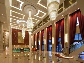 Um hall amplo com uma escadaria imponente, grandes lustres e um balcão de recepção.
