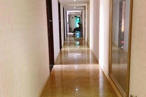 Corredor comprido e estreito com piso brilhante e refletivo, e uma pessoa sentada num banco ao longe.
