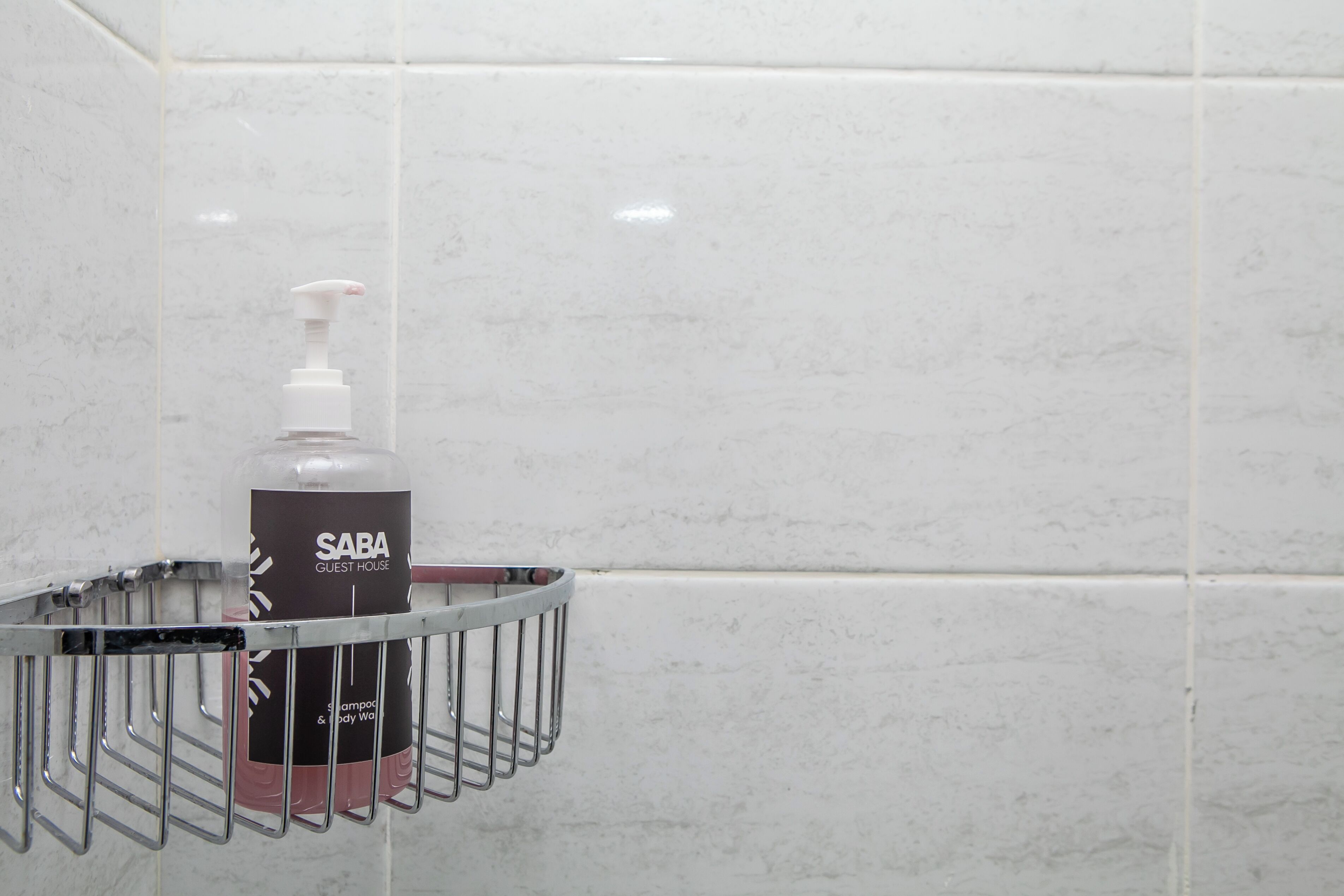 Casa de banho com parede de mármore, base de chuveiro em metal e um frasco de shampoo e gel de banho SABA.