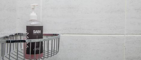 Casa de banho com parede de mármore, base de chuveiro em metal e um frasco de shampoo e gel de banho SABA.