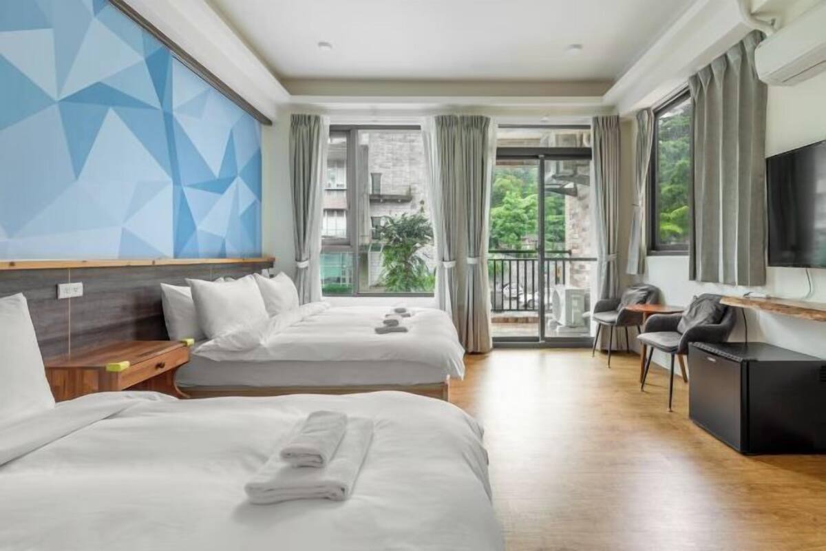 Quarto de hotel com duas camas, televisão, escrivaninha e varanda com vista.