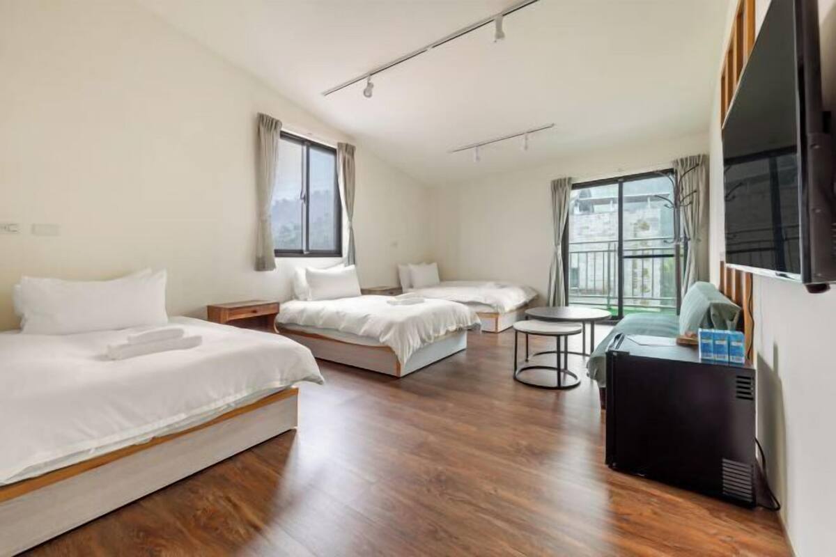 Quarto de hotel com duas camas, uma mesa pequena, televisão e varanda com vista.