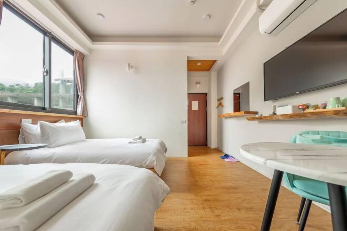 Quarto de hotel com duas camas, televisão, mesa e janela.