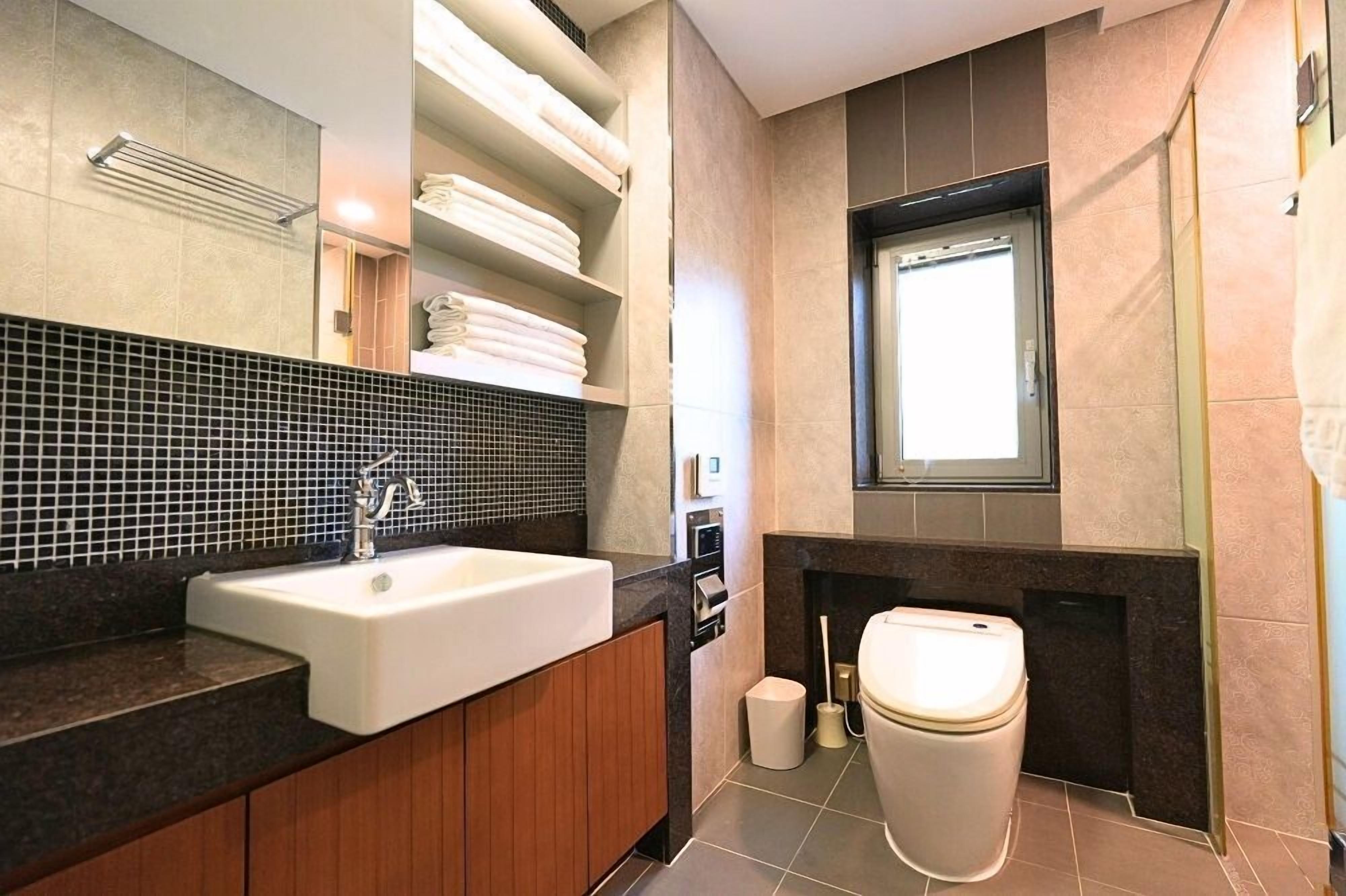 Uma casa de banho moderna com uma pia grande, um espelho, um porta-toalhas, uma sanita e uma janela.