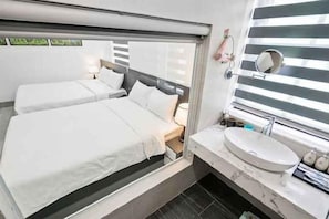 Quarto de hotel moderno com uma cama grande, banheiro com pia redonda e janela com persianas.