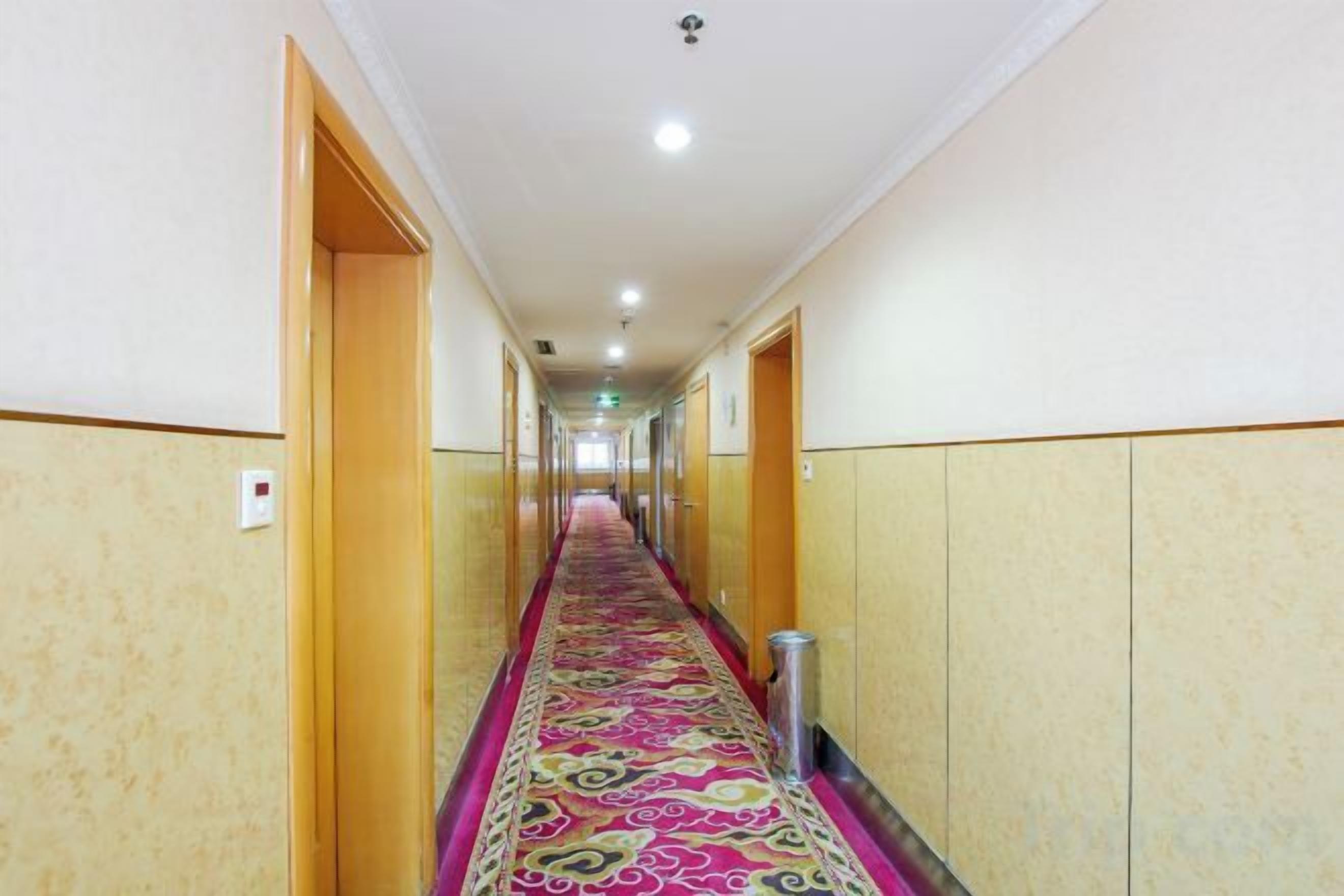 Corredor de hotel com piso coberto por carpete, portas em ambos os lados e uma lixeira.