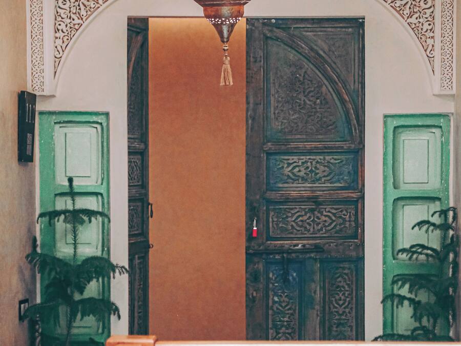 Uma escadaria com grades brancas ornamentadas, uma porta verde com entalhes detalhados e um candeeiro pendente.