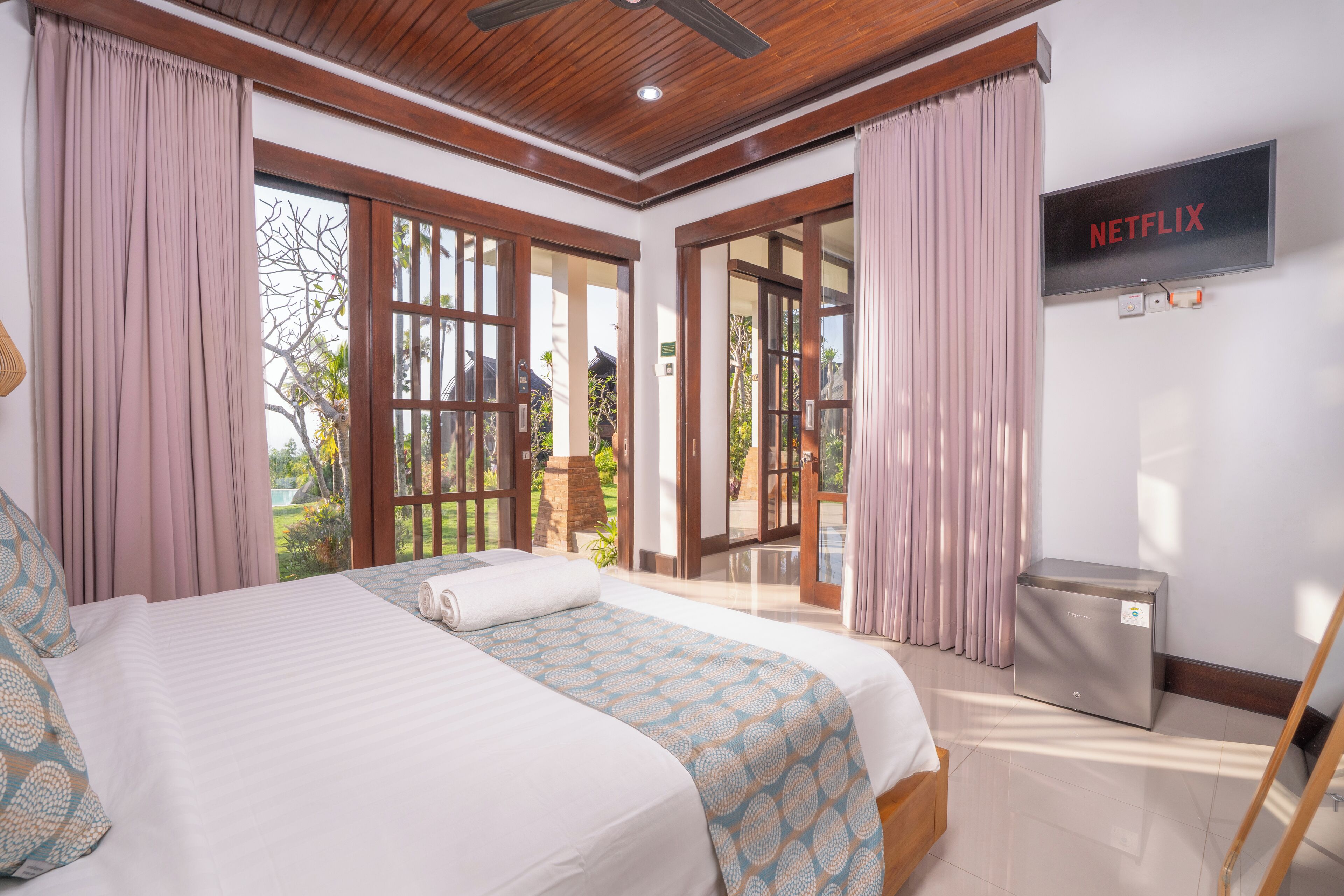 Quarto de hotel com cama, televisão na parede e vista para o exterior pelas janelas.