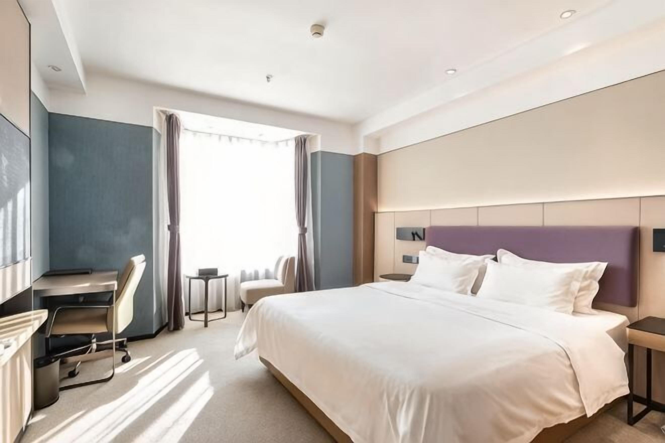 Quarto de hotel com cama, escrivaninha, cadeira e vista para o exterior.