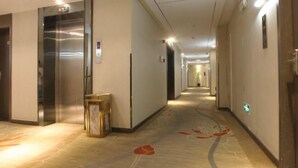 Corredor de hotel com piso de mármore, uma lixeira e um elevador.