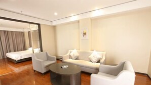 Quarto de hotel moderno com uma cama, dois sofás, uma mesa de centro e um espelho grande.