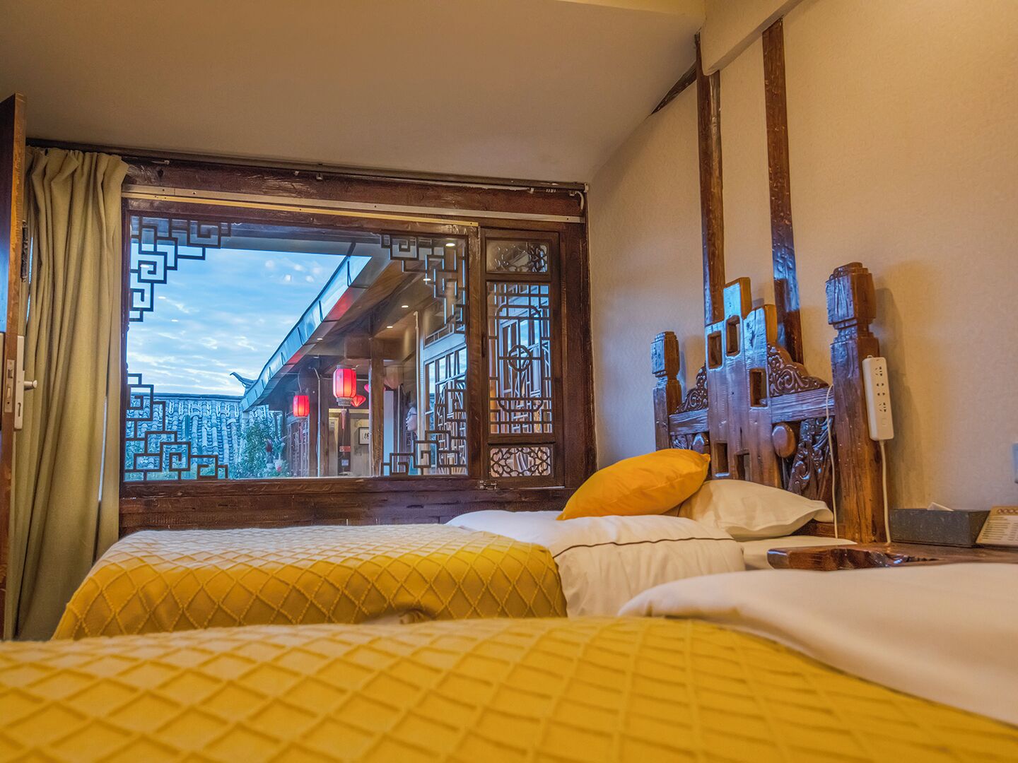 Quarto de hotel com duas camas, cabeceira de madeira e janela com design tradicional em treliça chinesa.