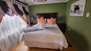 Uma cama bem arrumada com um edredom branco e duas almofadas fofas, piso de madeira, parede verde e luminária no teto.