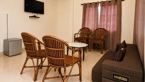 Uma sala de estar com sofá, duas poltronas, uma mesinha, televisão e geladeira.