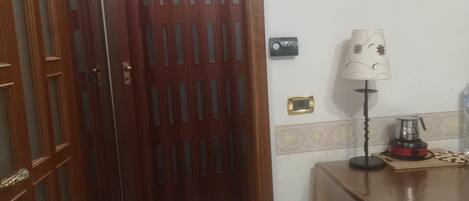 Um quarto com porta de madeira, uma pequena mesa com abajur e uma cadeira.