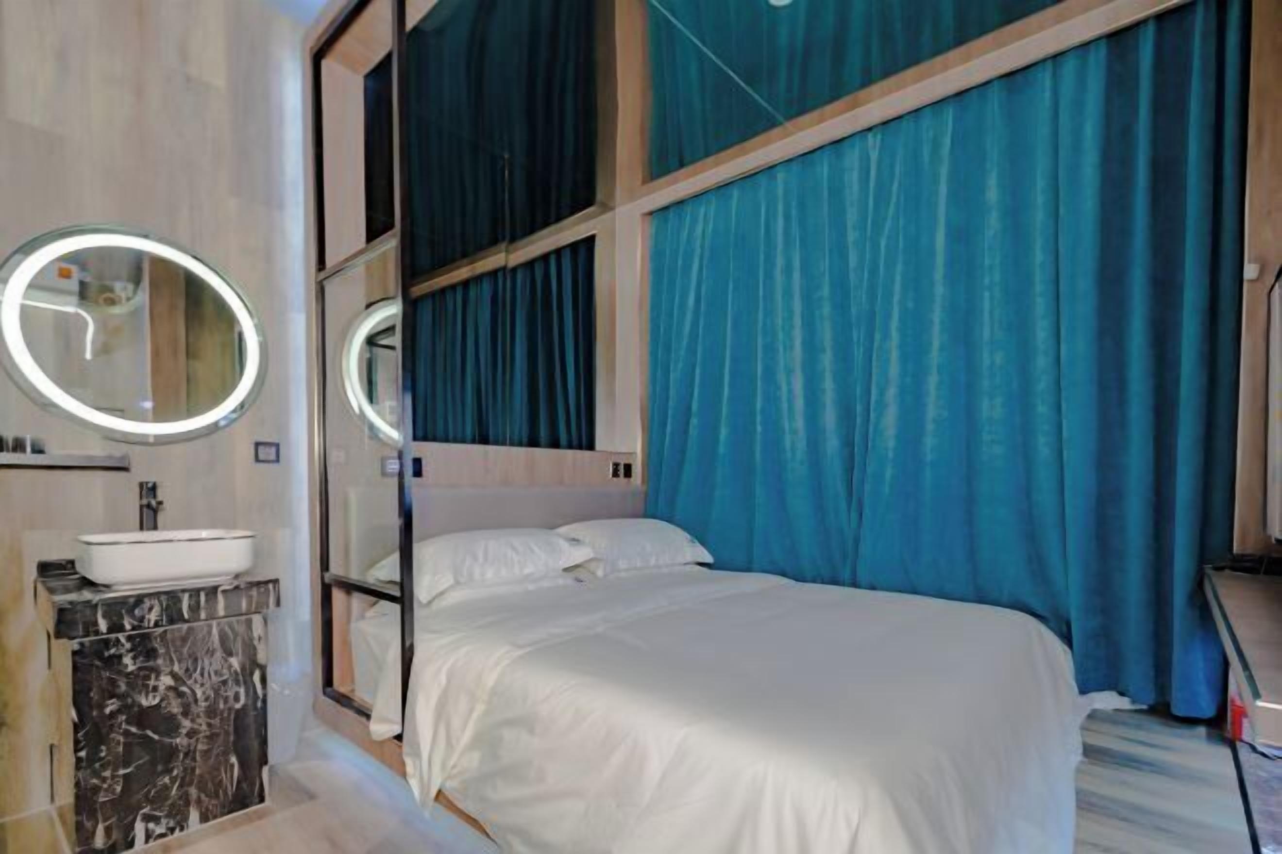 Quarto de hotel moderno com cama, toucador com espelho e uma grande janela com cortinas.
