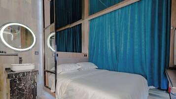 Quarto de hotel moderno com cama, toucador com espelho e uma grande janela com cortinas.
