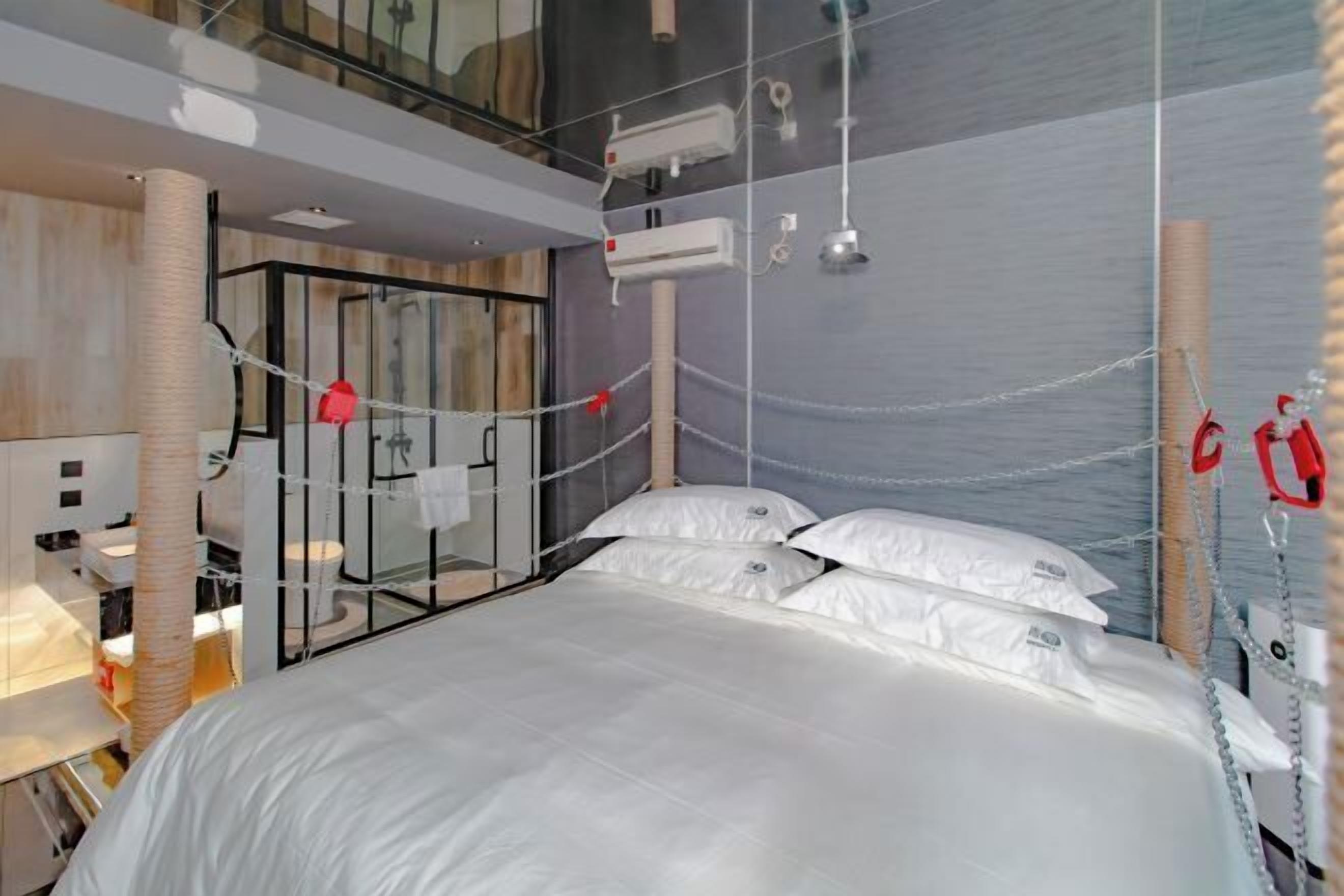 Quarto de hotel moderno com uma cama grande, divisória de vidro e vista para a cidade.