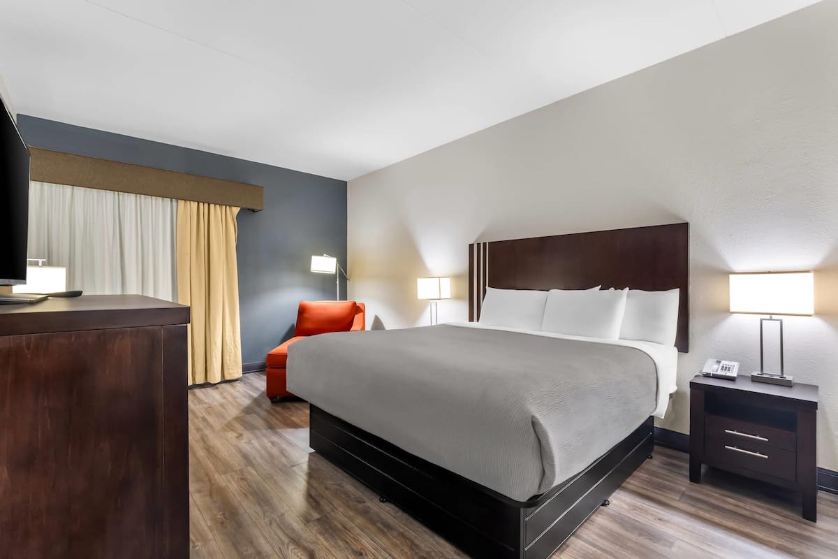Quarto de hotel com cama, escrivaninha, cadeira e mesa de cabeceira com abajur.