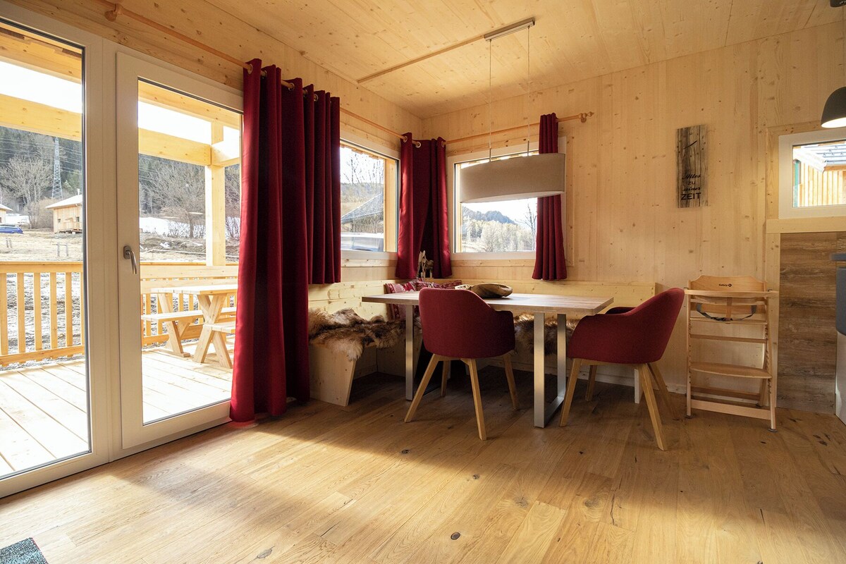 Interior de uma cabana de madeira com uma mesa de jantar, duas cadeiras e um banco.