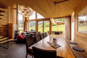Uma ampla sala de jantar com uma longa mesa de madeira, várias cadeiras e uma grande janela com vista para o exterior.