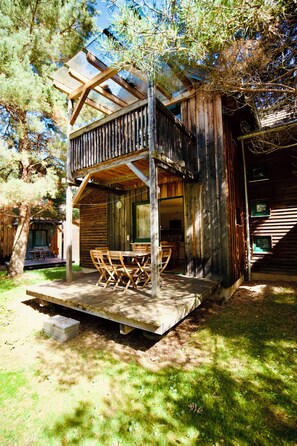 Uma cabana de madeira com varanda, área de jantar com cadeiras e mesa, e um espaço de estar ao ar livre coberto.