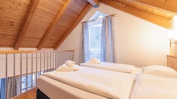 Quarto com duas camas, vigas de madeira no teto, janela com cortinas e varanda com guarda-corrimão.