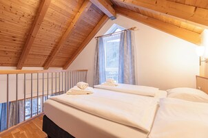 Quarto com duas camas, vigas de madeira no teto, janela com cortinas e varanda com guarda-corrimão.