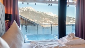 Quarto de hotel com cama, hidromassagem e vista para as montanhas.