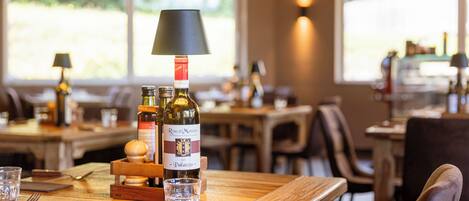 Interior de restaurante com mesas, cadeiras e uma garrafa de vinho em destaque.