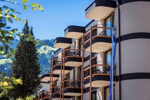 Um hotel com várias andares, varandas, grandes janelas e montanhas ao fundo.