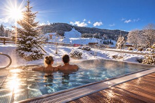 Um casal em uma banheira de hidromassagem com montanhas nevadas ao fundo.