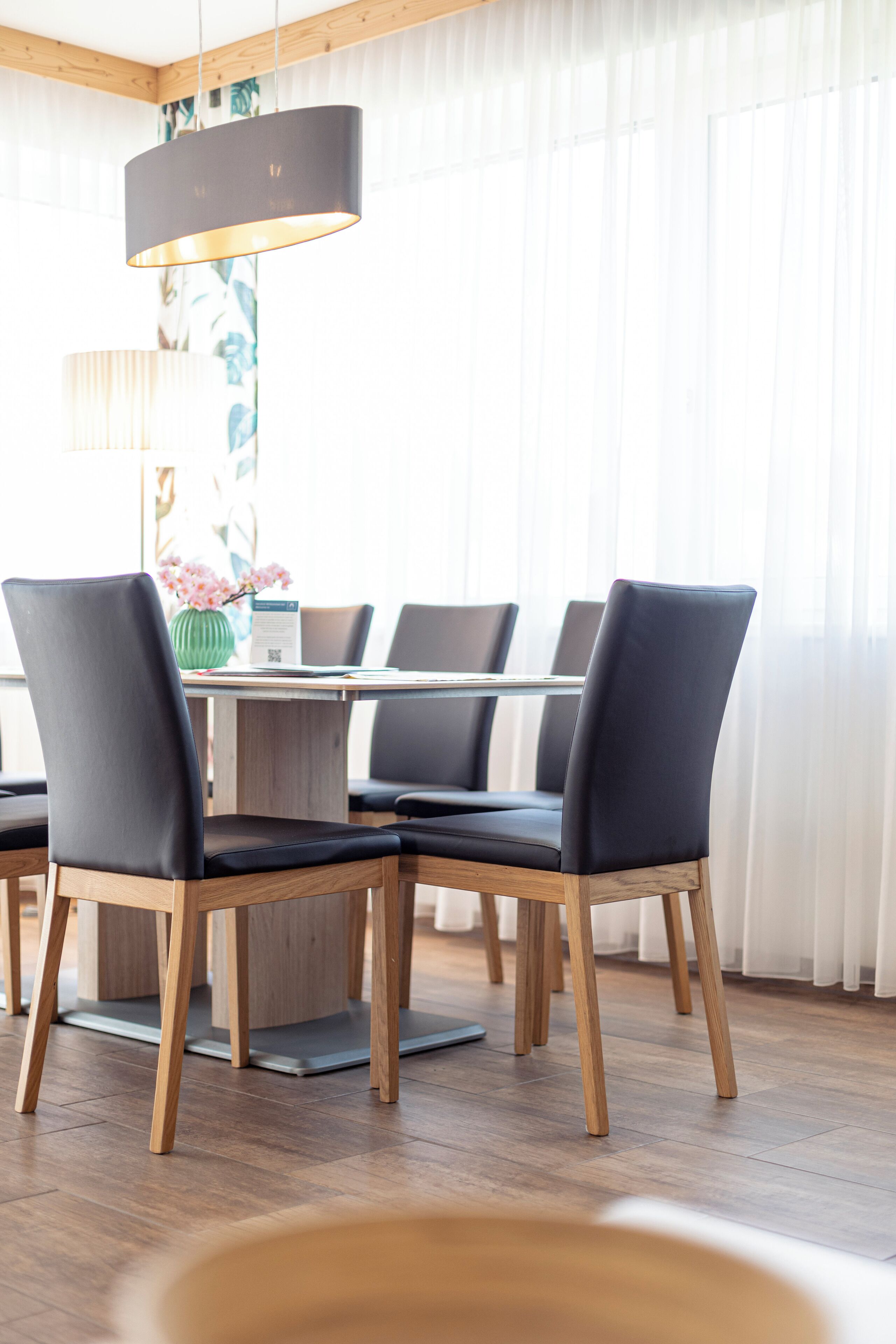 Uma área de jantar com uma mesa de madeira, cadeiras pretas e uma luminária pendente.