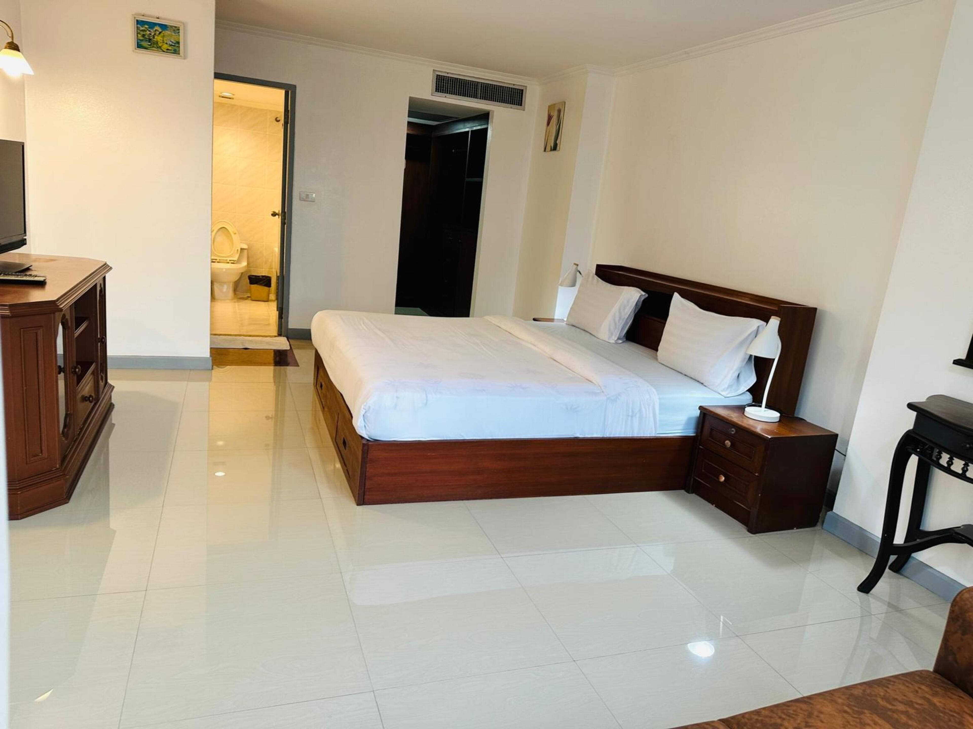 Quarto de hotel com cama de madeira, mesa de cabeceira, escrivaninha e uma cadeira.