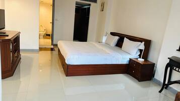 Quarto de hotel com cama de madeira, mesa de cabeceira, escrivaninha e uma cadeira.