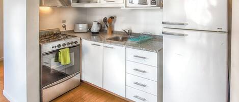 Cozinha compacta com armários brancos, fogão de aço inoxidável, micro-ondas e geladeira.