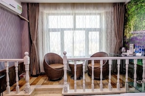 Quarto com varanda, cadeiras de vime, uma pequena mesa e vista para uma parede verde.