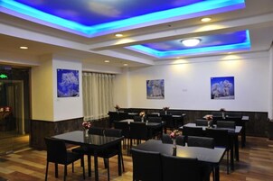 Restaurante com várias mesas e cadeiras, iluminação azul no teto e quadros nas paredes.