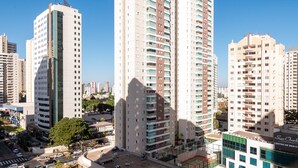 Um edifício residencial alto com várias varandas, quadra esportiva no terraço e um prédio comercial visível com sinalização.