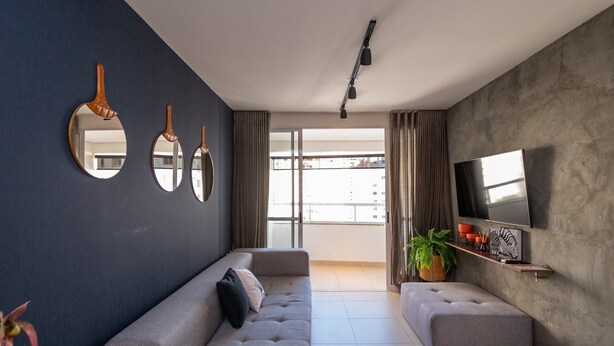 Uma sala de estar moderna com um sofá cinza, uma TV de tela plana na parede e três espelhos fixados na parede.