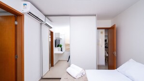 Quarto de hotel com cama, escrivaninha, espelho, televisão e ar condicionado.