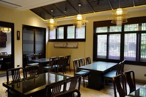 Uma sala de jantar com mesas, cadeiras, janelas amplas e luminárias pendentes.