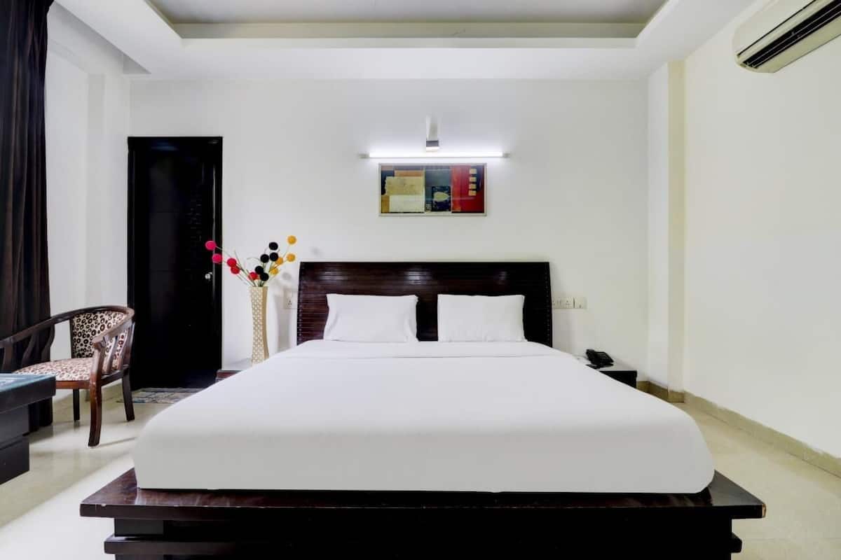 Quarto de hotel com cama grande, mesa de cabeceira, uma cadeira, uma obra de arte na parede e uma porta.