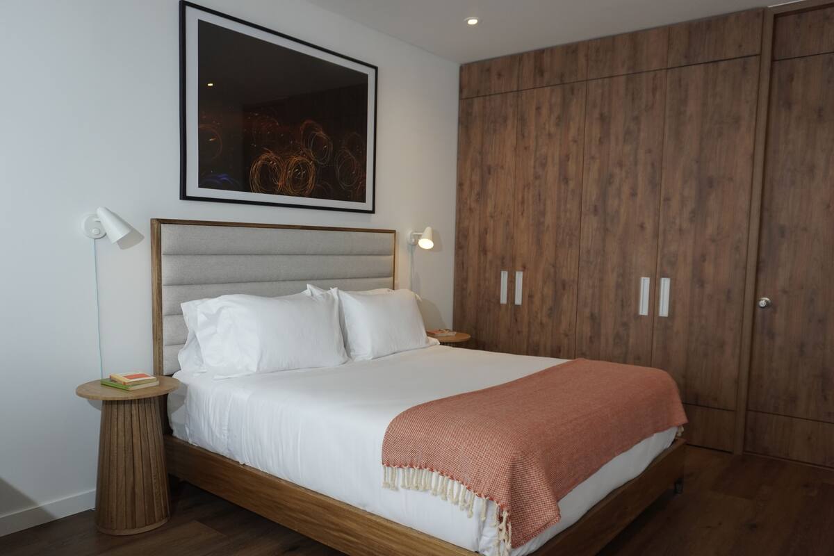 Quarto bem organizado com cama, luminárias de cabeceira, uma mesa redonda e um guarda-roupa.