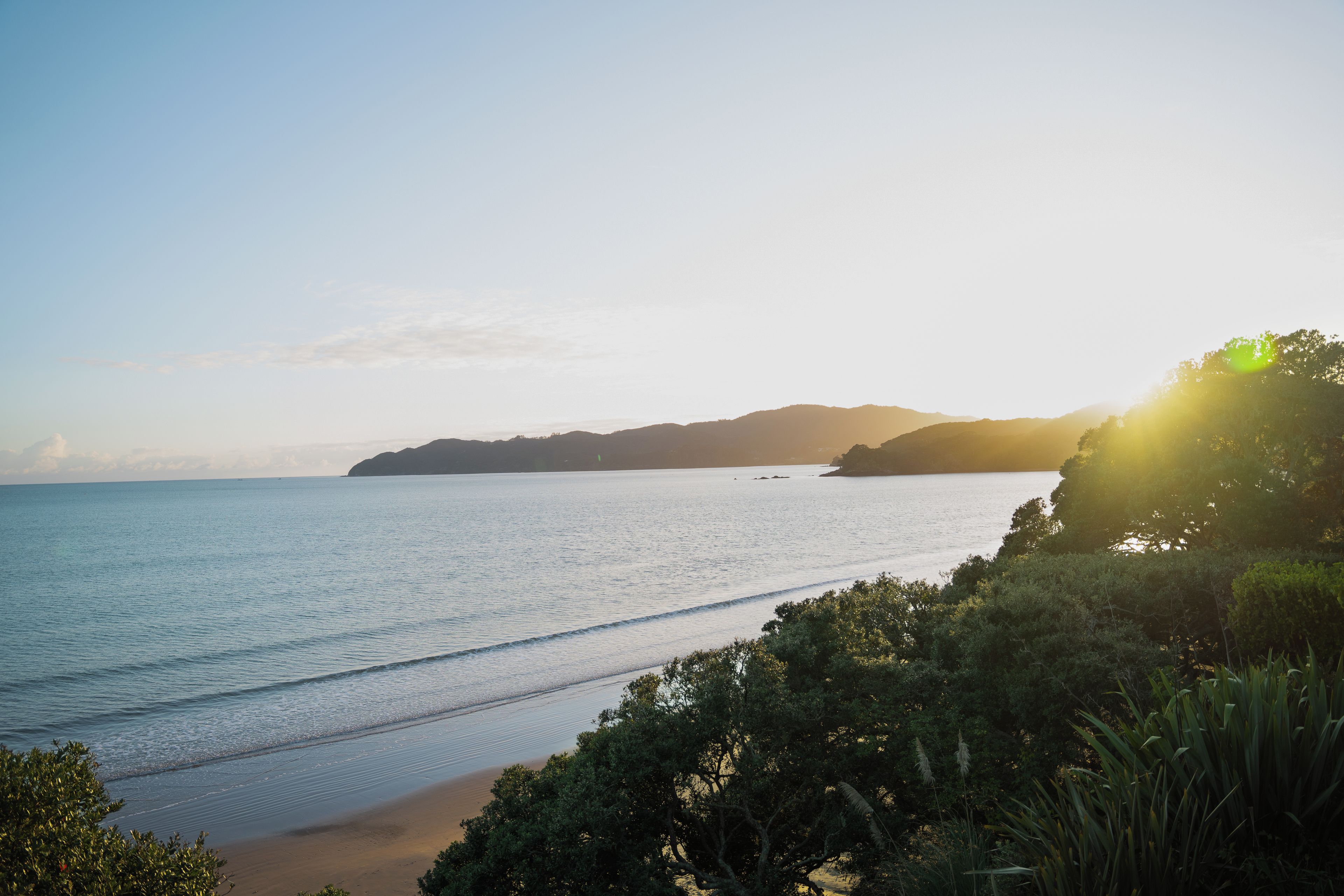 Paisagem costeira com praia, oceano e colinas ao longe.