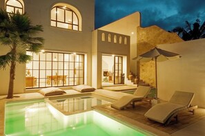 Uma área de piscina com espreguiçadeiras e guarda-sóis, uma escadaria e um espaço de refeições com mesas e cadeiras.