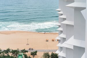 Vista da praia a partir de uma varanda de hotel, com areia, ondas do oceano e alguns guarda-sóis.