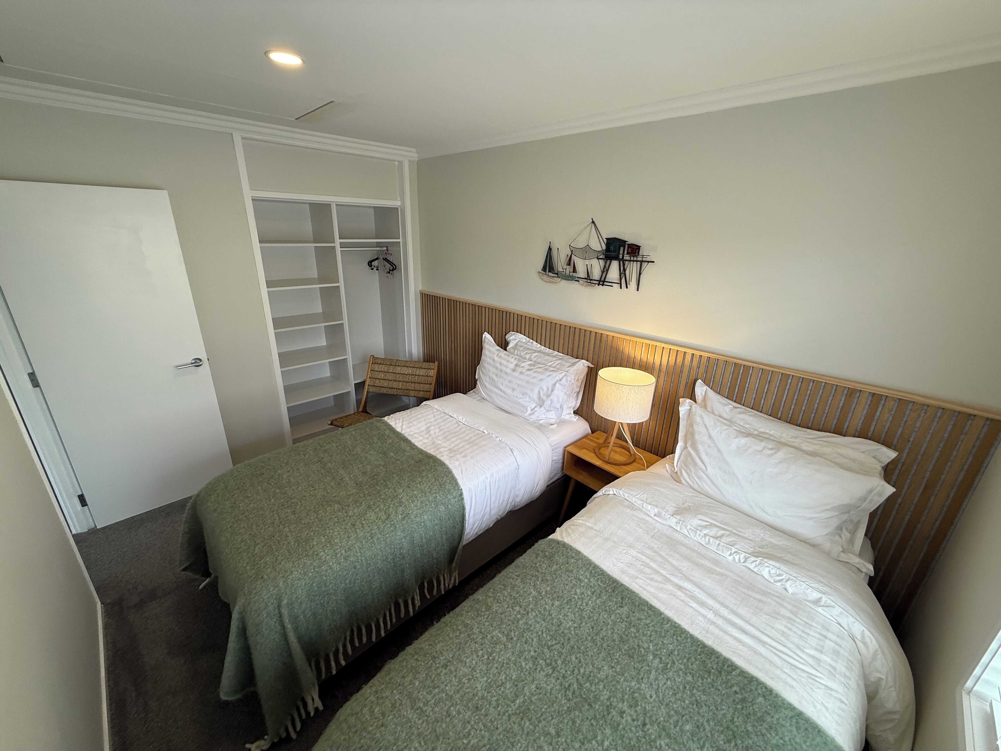 Quarto de hotel com duas camas, um closet espaçoso e uma mesa de cabeceira com abajur.