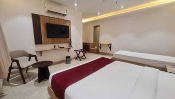 Quarto de hotel com uma cama grande, televisão na parede, escrivaninha e uma cadeira.