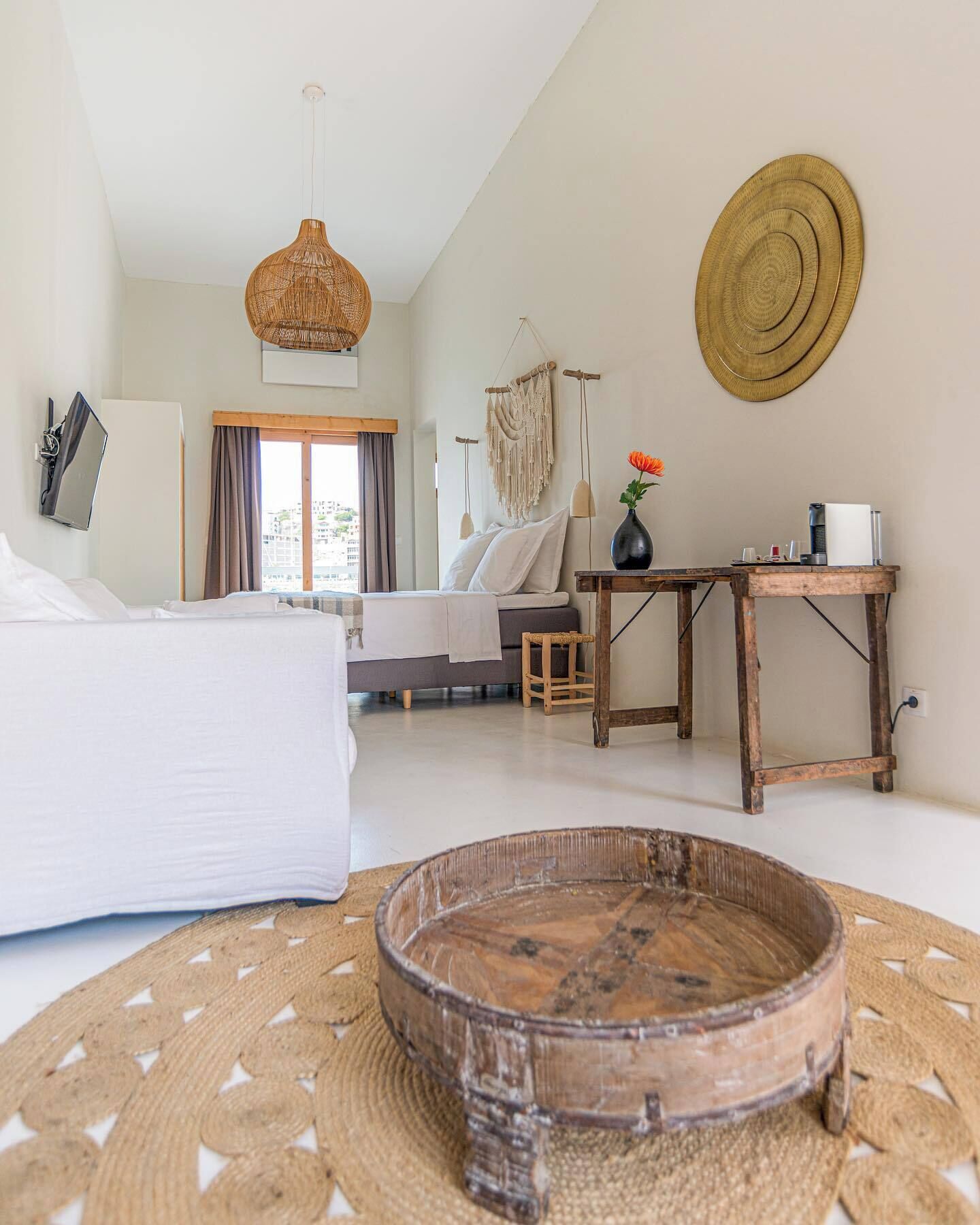 Quarto de hotel moderno com cama, escrivaninha, luminária pendente e vista para a cidade.
